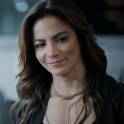 A Woman With Long Hair Wearing A Black Leather Jacket And Gold Necklace Smiling At The Camera