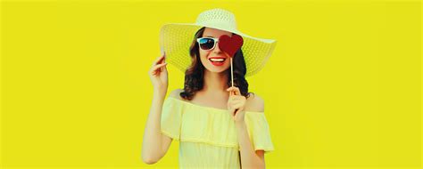 노란색 배경에 여름 밀짚 모자를 쓰고 빨간 달콤한 하트 모양의 롤리팝을 가진 행복한 미소 짓는 젊은 여성의 초상화 20 29세에 대한 스톡 사진 및 기타 이미지 Istock