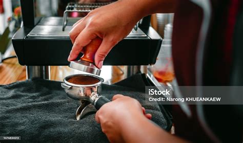 포터필터를 들고 있는 바리스타와 에스프레소 커피를 만드는 커피 탬퍼의 손 바리스타는 커피숍에서 탬퍼를 사용하여 분쇄 커피를 압착합니다 갈색에 대한 스톡 사진 및 기타 이미지