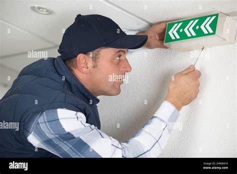 A Male Worker Fixing An Emergency Exit Sign Stock Photo Alamy