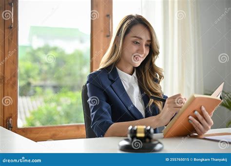 Successful Asian Female Lawyer Reading A Law Book At Her Office Desk