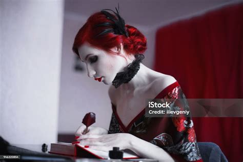 목욕 가운과 복고풍 메이크업에 붉은 곱슬 머리를 가진 여자는 책에서 씁니다 창백한 피부 파란 눈 밝은 특이 한 모습을 빨간 입술 및 치명적인 얼굴 빨간 머리 소녀 노아 여자