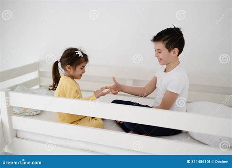 Brother And Sister Playing A Game Of Rock Scissors Paper On Bed At