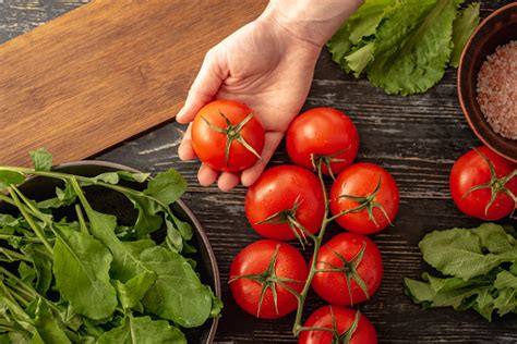 여자의 손이 잘 익은 빨간 토마토를 들고 있습니다 검은 테이블에는 토마토 Arugula 그린 샐러드 및 가벼운 비타민 야채
