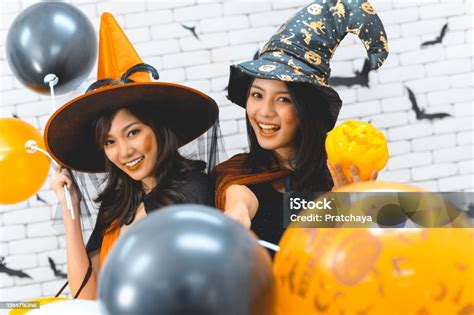 할로윈 파티를위한 검은 종이 박쥐 모양으로 장식 된 흰색 벽돌 배경에 풍선을 들고 마녀 할로윈 의상을 입은 두 명의 아름다운