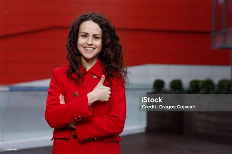 빨간 건물 배경에 엄지 손가락을 보여주는 빨간 정장에 예쁜 갈색 머리 곱슬 젊은 여자의 야외 초상화 간판에 대한 스톡 사진 및 기타 이미지 Istock