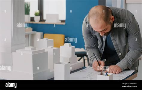 Close Up Of Architect Taking Notes On Blueprints Plan To Work On Building Model And Maquette