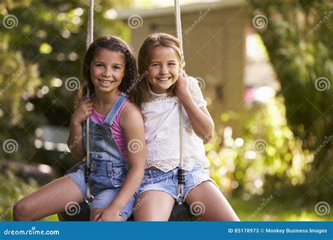 Portrait Of Two Girls Playing On Tire Swing In Garden Stock Image