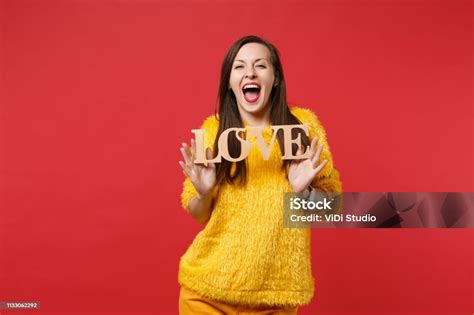 밝은 빨간색 벽 배경에 고립 된 나무 단어 편지 사랑을 유지 입 넓은 열려있는 노란 모피 스웨터에 재미 있는 젊은 여자 사람들은