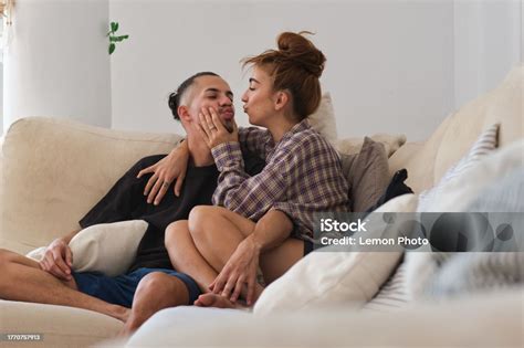라틴계 젊은 남녀 커플이 소파에 앉아 서로를 바라보며 농담을 하고 미소 짓는 모습의 일반 사진 커플에 대한 스톡 사진 및 기타