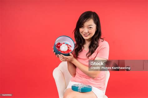 선물 상자를 들고 빨간 배경 위에 고립된 작은 하트로 흰 장미 꽃을 보여주는 아름다운 아시아 여성 발렌타인 데이 개념입니다