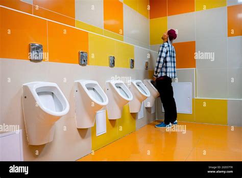 Young Man In The Public Toilet Standing Next To The Urinal In The