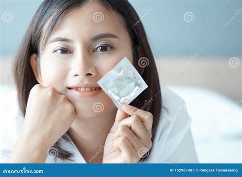 Close Up Woman Hand Holding Condom With Happy Face Lying On White Bed