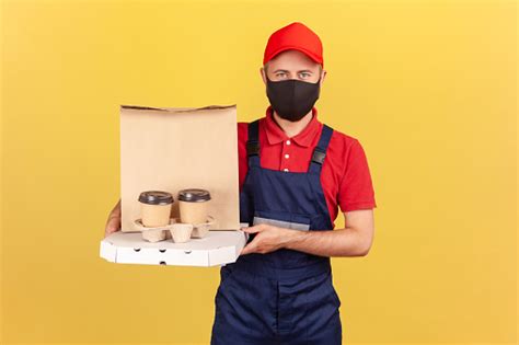제복을 입은 흑인 의료용 보호 마스크를 착용한 배달원은 검역소에서 음료와 음식 배달을 제공하는 피자와 함께 커피와 상자를 들고
