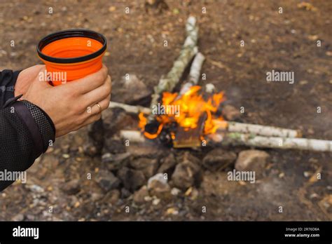 Hands Holding Orange Cup Of Tea Against Fireplace Background Picnic Concept Unfocused Bonfire