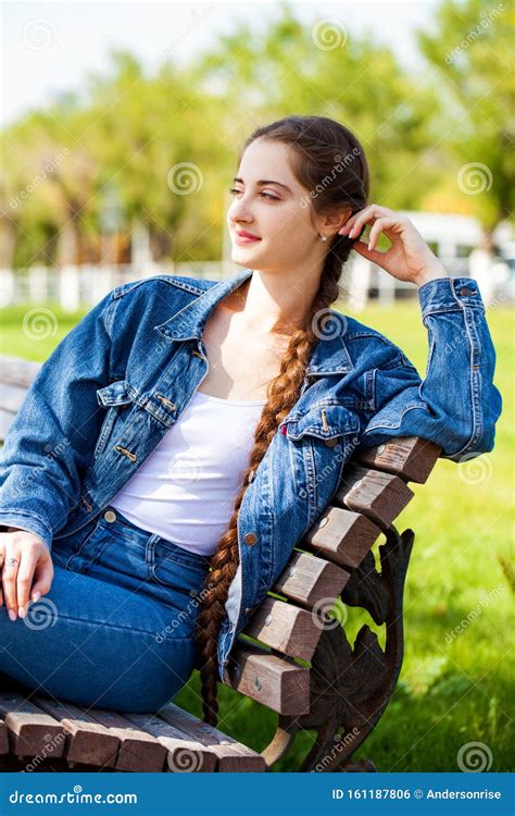 Beautiful Girl In A Denim Jacket Sits On A Bench In A Summer Park Stock