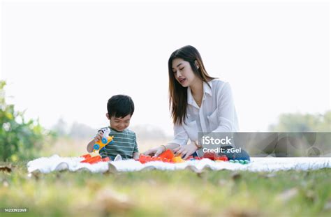 젊은 아시아 어머니와 귀여운 작은 아들의 초상화는 여름 공원에서 화창한 하루를 보내고 화려한 플라스틱 블록 장난감을 연주하는