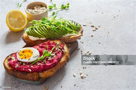 밝은 회색 배경에 크림 치즈 아보카도 비트 뿌리 후 머스 씨앗 계란 및 마이크로 그린 을 곁들인 통 곡물 토스트 건강 한 음식