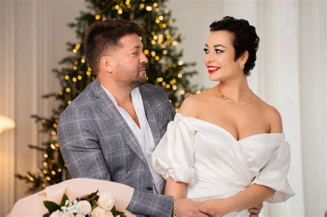 A Man And Woman Are Sitting Next To A Christmas Tree They Are Holding