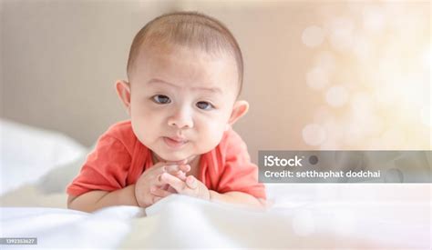 행복한 가족 귀여운 아시아 신생아는 빨간 셔츠를 입고 거짓말을하고 기어 다니며 하얀 침대에서 행복한 얼굴로 카메라를 바라 봅니다 건강한 생활방식에 대한 스톡 사진 및 기타