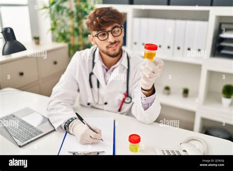 Young Arab Man Wearing Doctor Uniform Writing On Document Analysing Urine Test Tube At Clinic