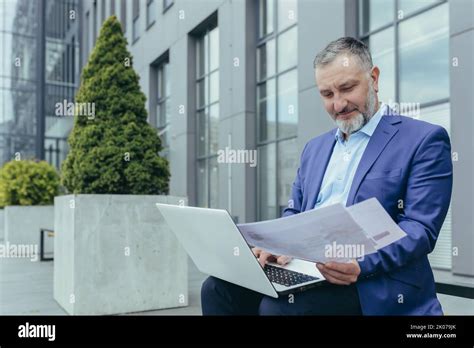 Senior Handsome Successful Male Engineer Architect In Suit Works With Laptop Documents Plan