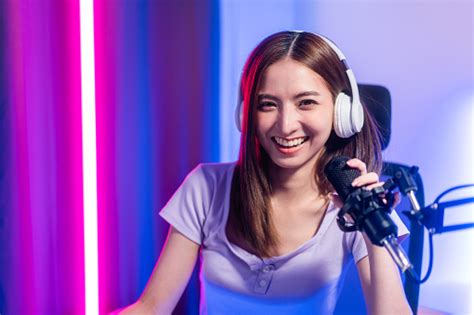 프로 게이머 거실에 컴퓨터 Pc가있는 의자에 앉아있는 젊은 아시아 예쁜 여자 행복한 여성 전문 스트리머 중국어 착용 헤드폰