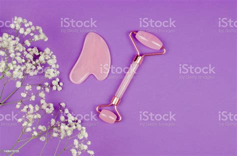 로즈 쿼츠 구아 샤 마사지 스크레이퍼와 석고 필라 꽃다발과 보라색 배경에 얼굴 마사지 롤러 노화 방지 치료 얼굴 관리 0명에
