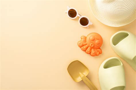 어린 아이와 함께 해변 휴양지를 최대한 활용하세요 부드러운 베이지색 배경에 문어 모래 곰팡이 삽 선글라스 모자 고무 슬리퍼가 있는 오버헤드 샷 가족 중심의 광고 또는 제안에