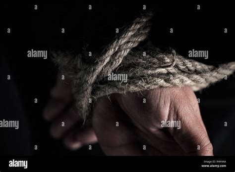 Closeup Of A Man With His Hands Tied Behind His Back With Rope Against
