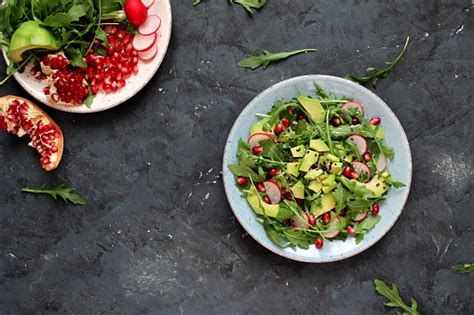 어두운 배경에 샐러드를 만들기 위한 성분 접시 아보카도 Arugula 석류 무와 참 깨 야채 샐러드 건강한 생활방식에 대한 스톡