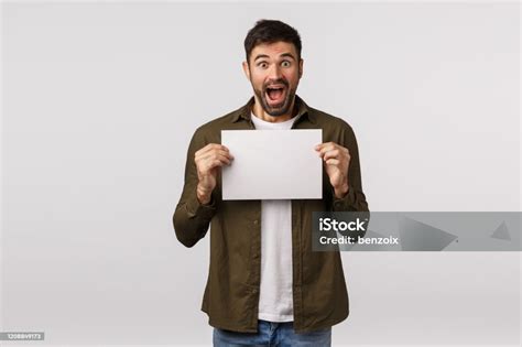 당신은 이것을 보아야합니다 흥분 행복하고 쾌활한 남자 코트에 빈 종이를 들고 즐겁게 미소 카메라 기절 보고 흥분 또는 매혹적인