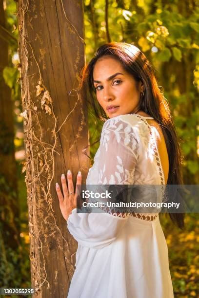 라이프 스타일 직선 머리 라틴갈색 갈색 머리 소녀 에 아름 다운 흰색 드레스 에 공원에서 자연 카메라를 바라보는 녹색 잎이 있는 나무에 기대어 있는 센수알 초상화 패션