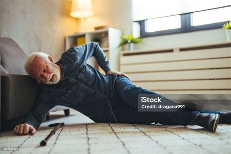 아픈 노인이 거실에서 나무 지팡이를 짚고 혼자 집에 걸려 넘어져 바닥에 누워 있습니다 떨어짐에 대한 스톡 사진 및 기타 이미지