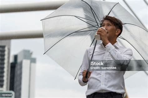 장마철에는 커피와 우산 한 잔을 들고 있는 사업가가 카피 스페이스가 있는 도시에 서있는 동안 비가 내리는 전경을 들고 있습니다 건물과 야외에서 뜨거운 커피를 마시는 직원