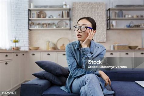 거실의 소파에 앉아있는 안경을 쓰고 생각하는 젊은 아름다운 아시아 여성 20 24세에 대한 스톡 사진 및 기타 이미지 20