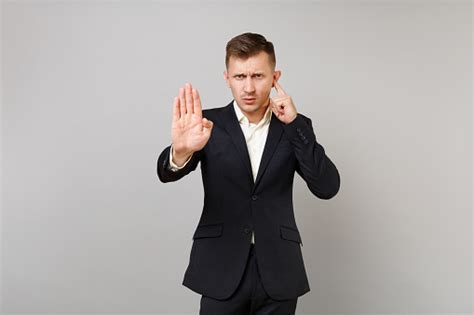 우려 젊은 비즈니스 남자가 고전적인 검은 양복 손가락으로 귀를 덮고 손바닥 회색 배경에 고립 중지 제스처를 보여주는 있다 성과