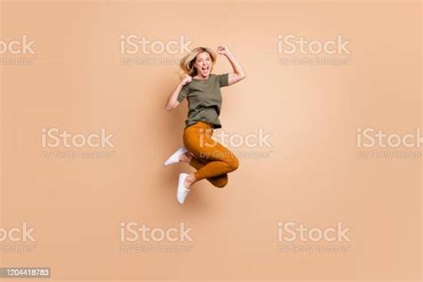 미친 여자 점프 높은 경쟁 분위기의 전체 길이 프로필 사진 최고의 승리를 축하 녹색 티셔츠 노란색 바지 고립 된 베이지 색 배경