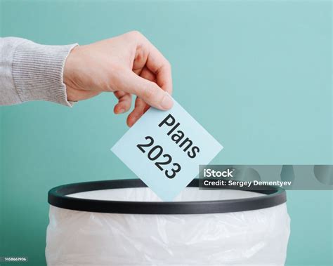 쓰레기통에 2023년 계획이 새겨진 스티커 메모를 던지는 손의 클로즈업 창의적인 아이디어는 산산조각난 꿈 성취되지 않은 계획
