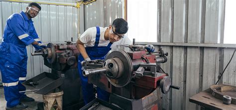 금속 선반 기계를 사용하는 다양성 정비사 또는 금속 세공인은 자동차 수리 차고에서 자동차 디스크 브레이크를 연마합니다 자동차