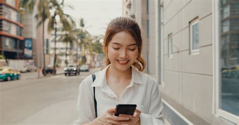 스마트폰을 사용하여 패션 사무복을 입고 아침에 도시의 현대 도시에서 혼자 야외를 걷는 동안 문자 메시지를 입력하는 성공적인 젊은