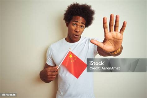 중국 국기를 들고 있는 젊은 아프로 미국인 남자가 고립 된 흰색 배경 위에 서 있고 진지하고 자신감있는 표정으로 정지 표지판을