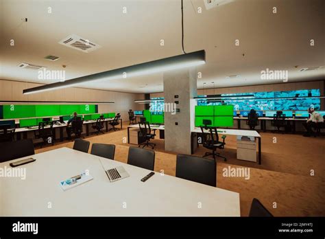 Group Of Security Data Center Operators Working In A CCTV Monitoring Room Looking On Multiple