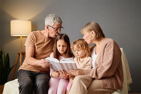 네 명의 가족 구성원이 따뜻하고 매력적인 거실에서 책을 읽으며 함께 조용한 시간을 즐깁니다 조부모는 어린 손주들과 관계를 맺으며 이야기에 대한 사랑을 키웁니다 가족에 대한