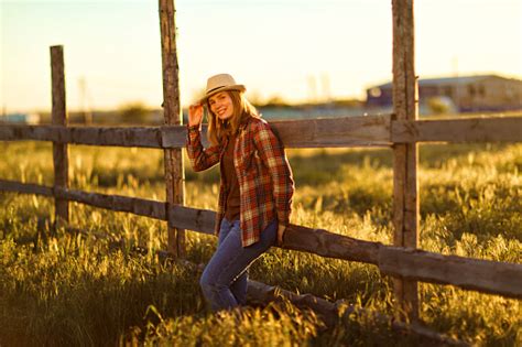 마을의 일몰에 울타리 근처에 서 모자와 격자 무늬 셔츠를 입은 여자 마을에 대한 스톡 사진 및 기타 이미지 마을 여성 여자 Istock