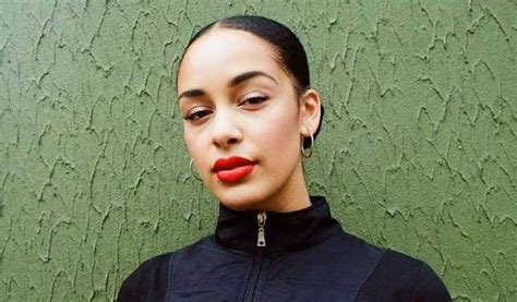 A Woman With Red Lipstick Standing In Front Of A Green Wall Wearing A