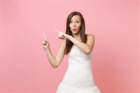 하얀 웨딩에서 놀된 신부 여자의 초상화는 서 부 입술 옆으로 파스텔 핑크 배경에 고립 된 인덱스 손가락을 가리키는 드레스 결혼식