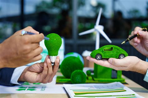 사무실 책상에서 열리는 회의는 주택 모델을 통한 팀워크와 전기 자동차 태양 전지 및 친환경 이니셔티브에 대한 토론에 중점을 두고 지속 가능성 및 환경 목표를 강조합니다 0에