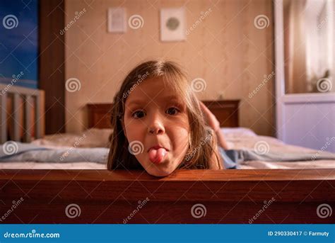 A Little Teenage Girl Is Playing Around On The Bed Sticking Her Tongue Out At The Camera Stock