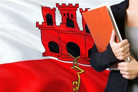 학습 언어 개념입니다 백그라운드에서 지브롤터 국기와 함께 서 있는 젊은 여자 책을 들고 교사 오렌지 빈 책 표지 교사 교육 관련